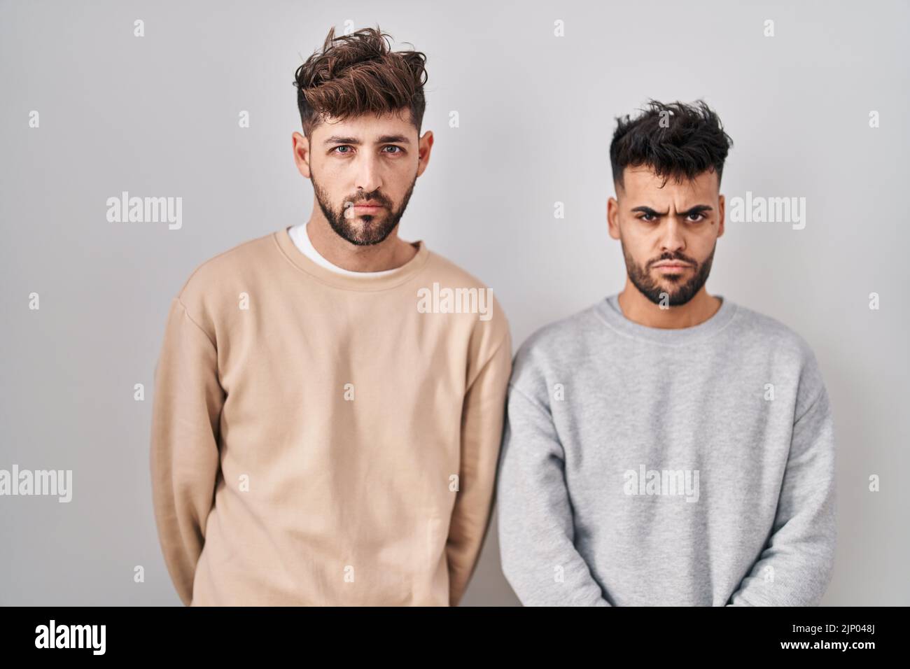 Young homosexual couple standing over white background skeptic and ...