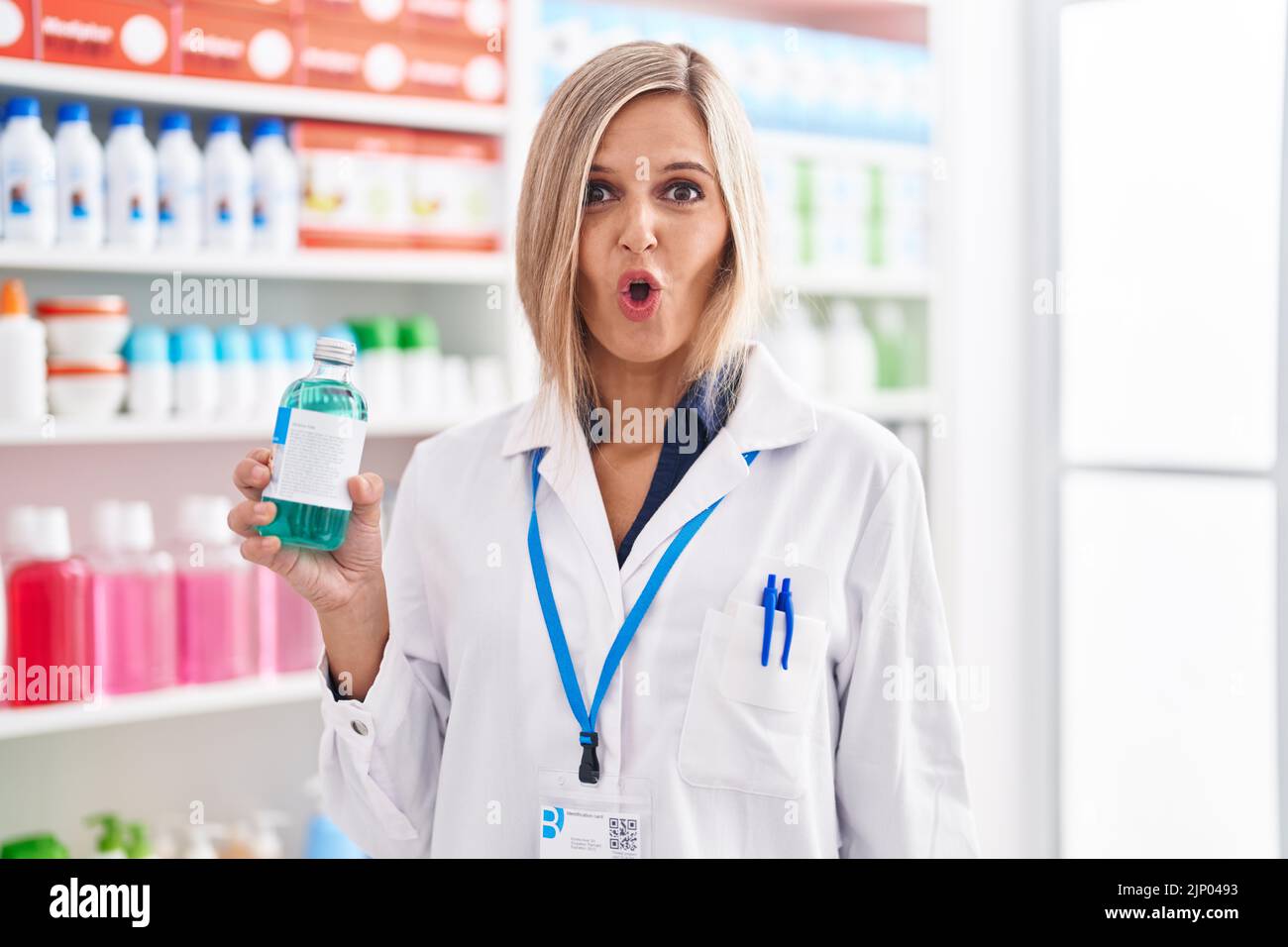 Blonde woman working at pharmacy drugstore holding syrup scared and ...