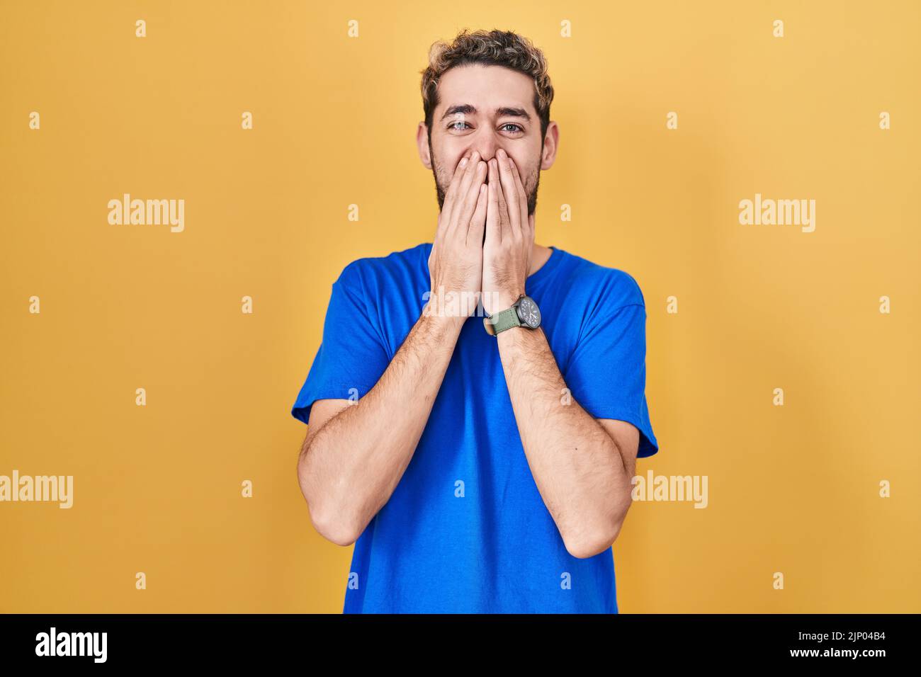 Hispanic man with beard standing over yellow background laughing and ...