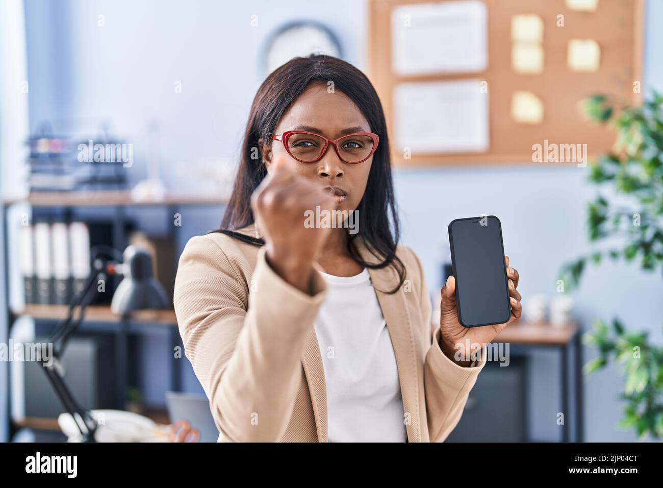 African young woman holding smartphone showing blank screen annoyed and ...