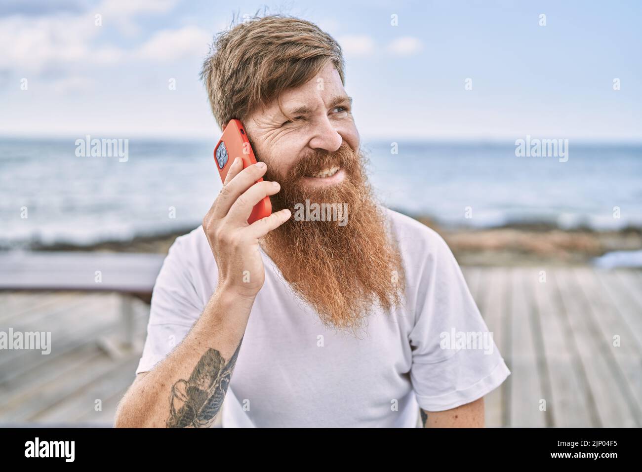 Young redhead man talking on the smartphone sitting on the bench at the ...