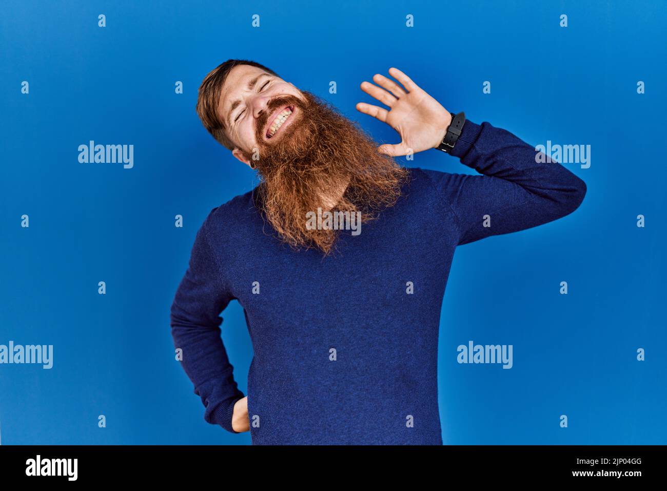 Redhead man with long beard wearing casual blue sweater over blue ...