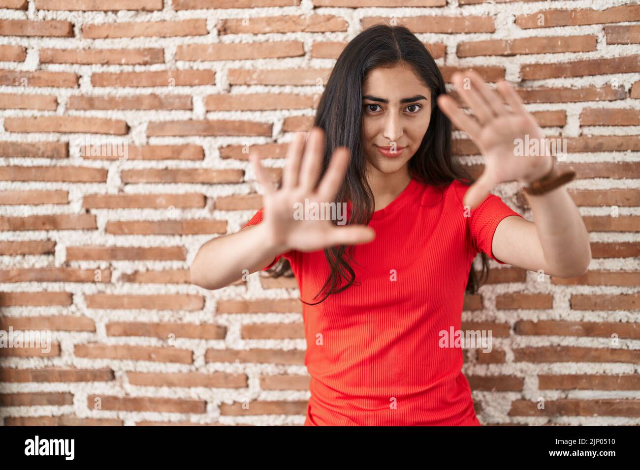 Young teenager girl standing over bricks wall doing frame using hands ...