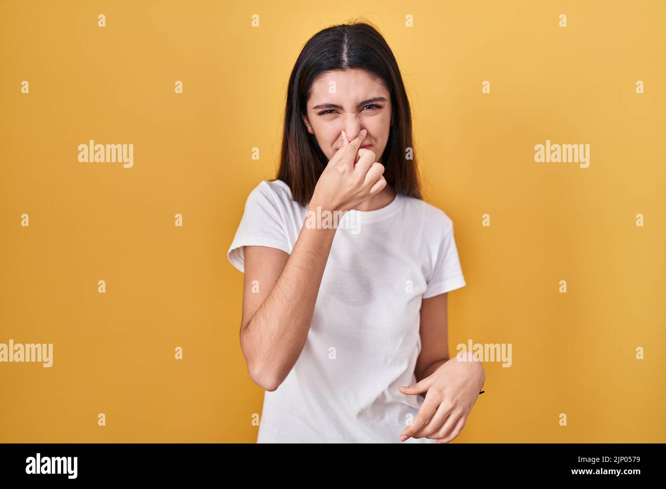 Young beautiful woman standing over yellow background smelling ...