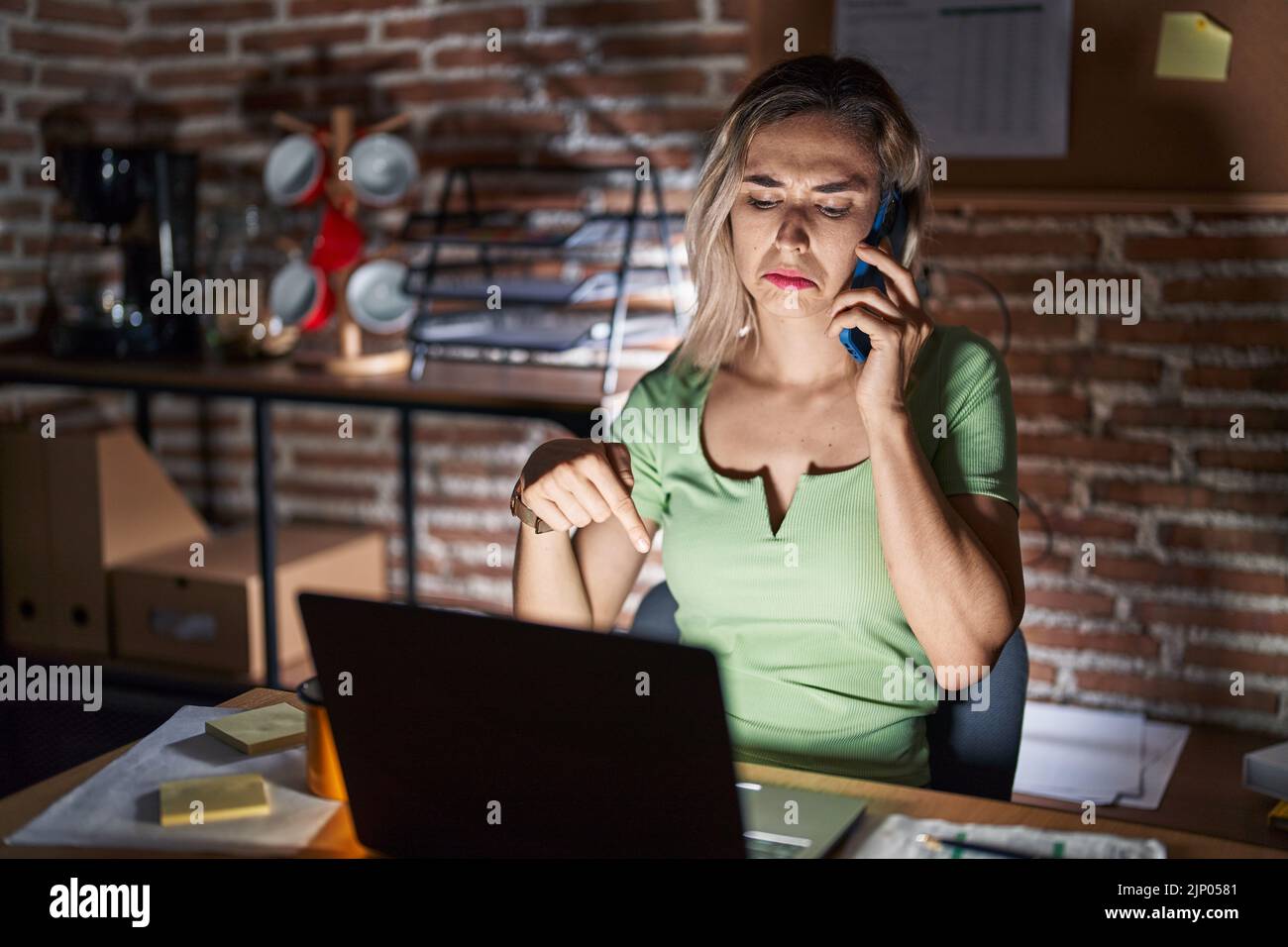 Young beautiful woman working at the office at night speaking on the ...