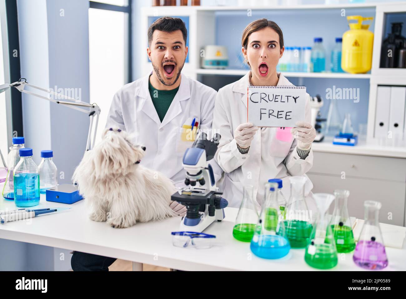 Young hispanic people working at scientist laboratory with dog afraid ...