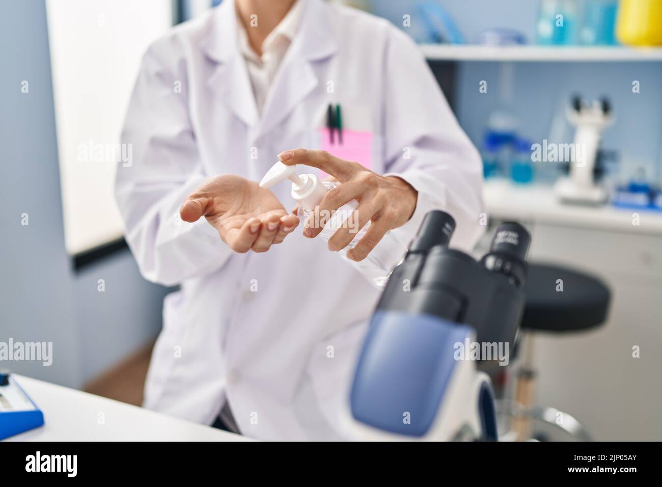 Young woman wearing scientist uniform using sanitizer hands gel at ...