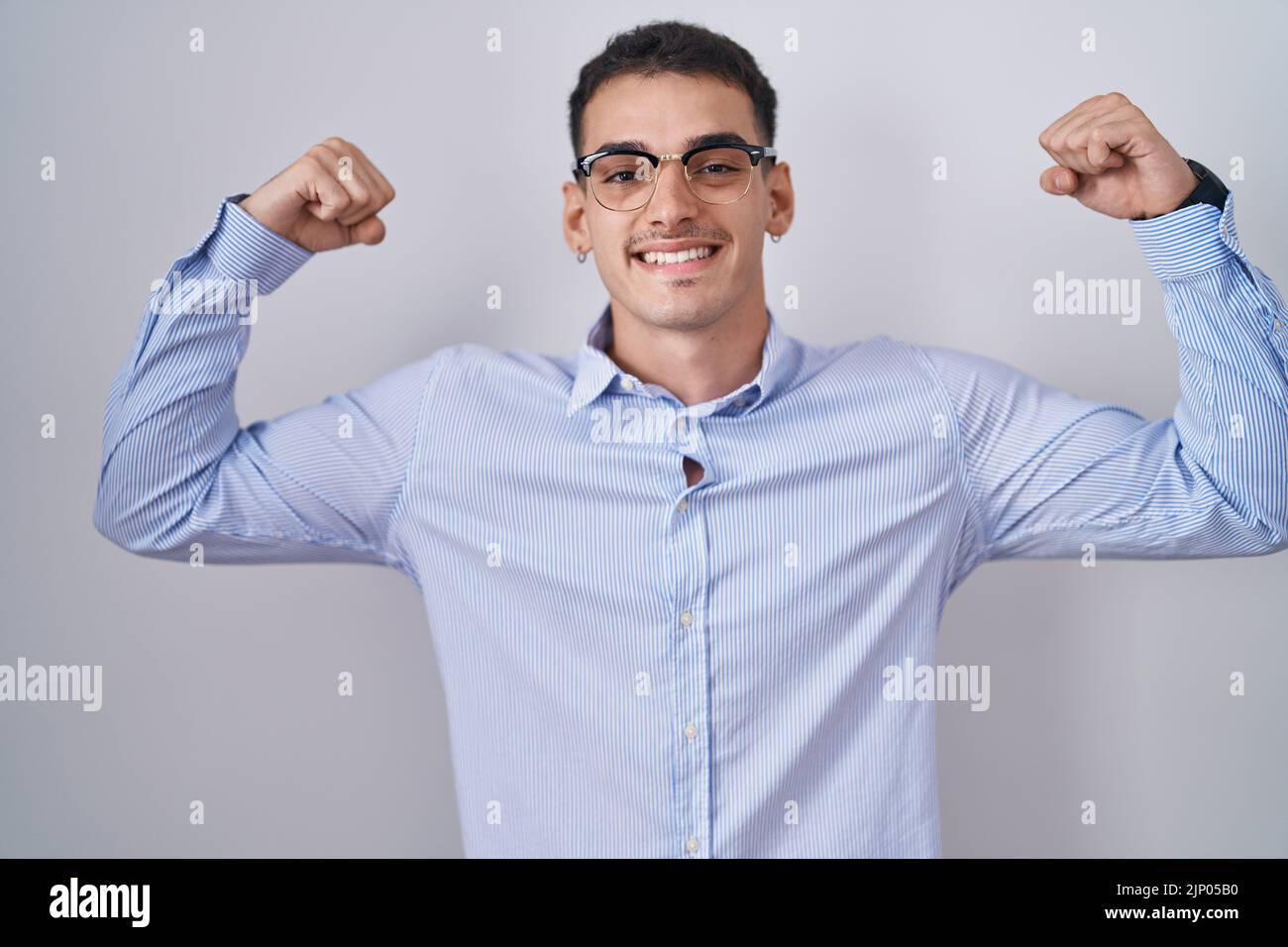 Handsome hispanic man wearing business clothes and glasses showing arms ...
