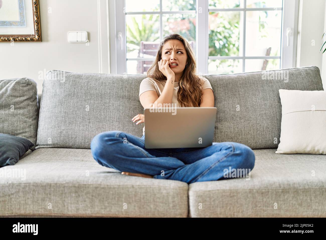 Beautiful young brunette woman sitting on the sofa using computer ...