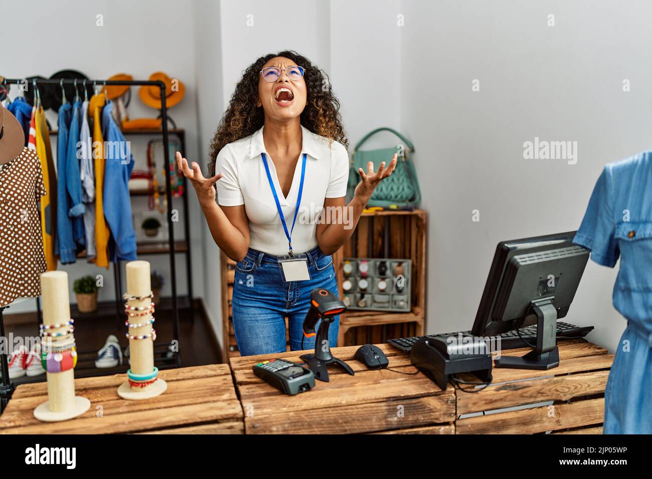 Beautiful hispanic woman working at clothing shop crazy and mad ...
