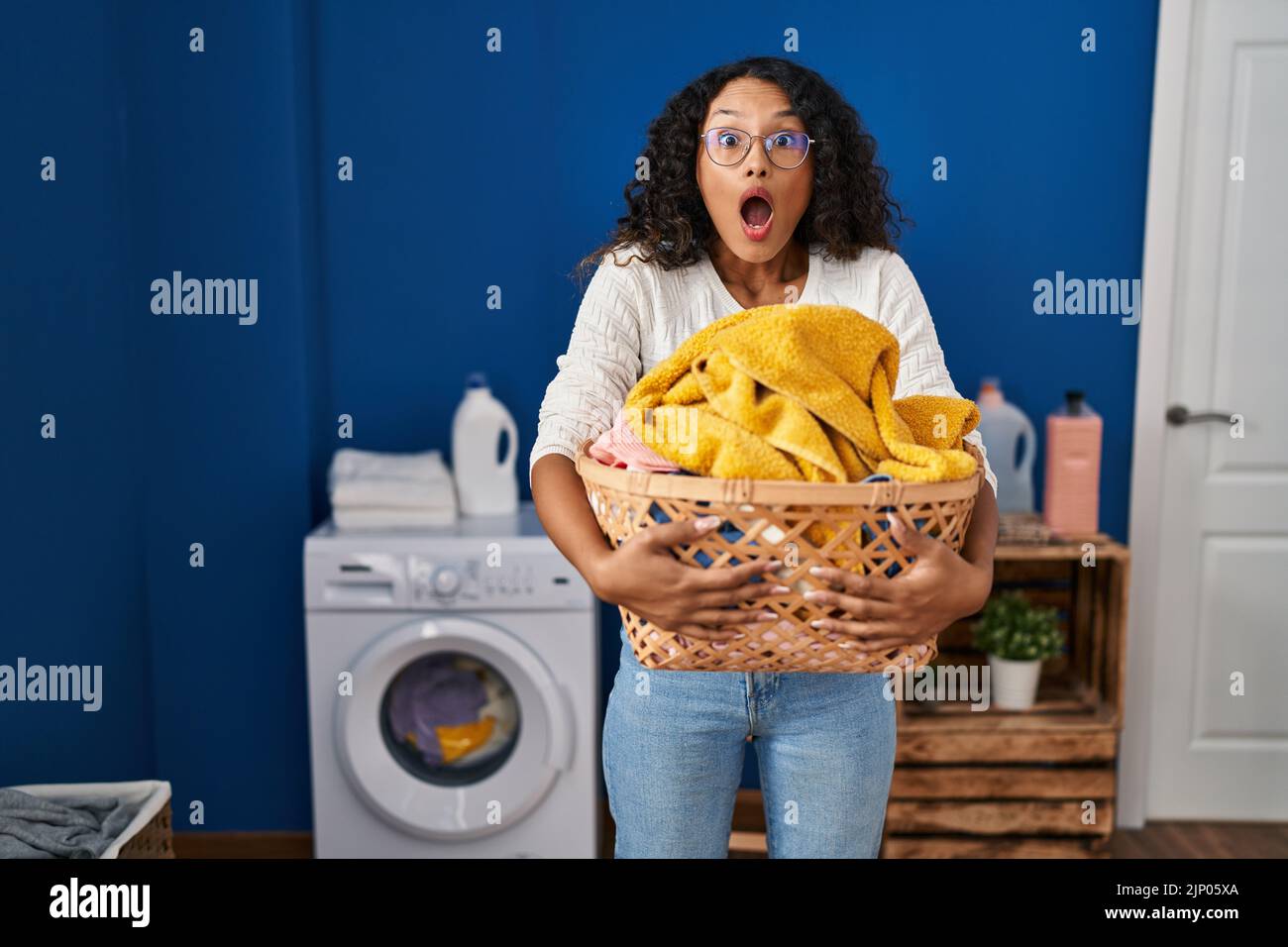 Young hispanic woman doing laundry holding wicker basket afraid and ...