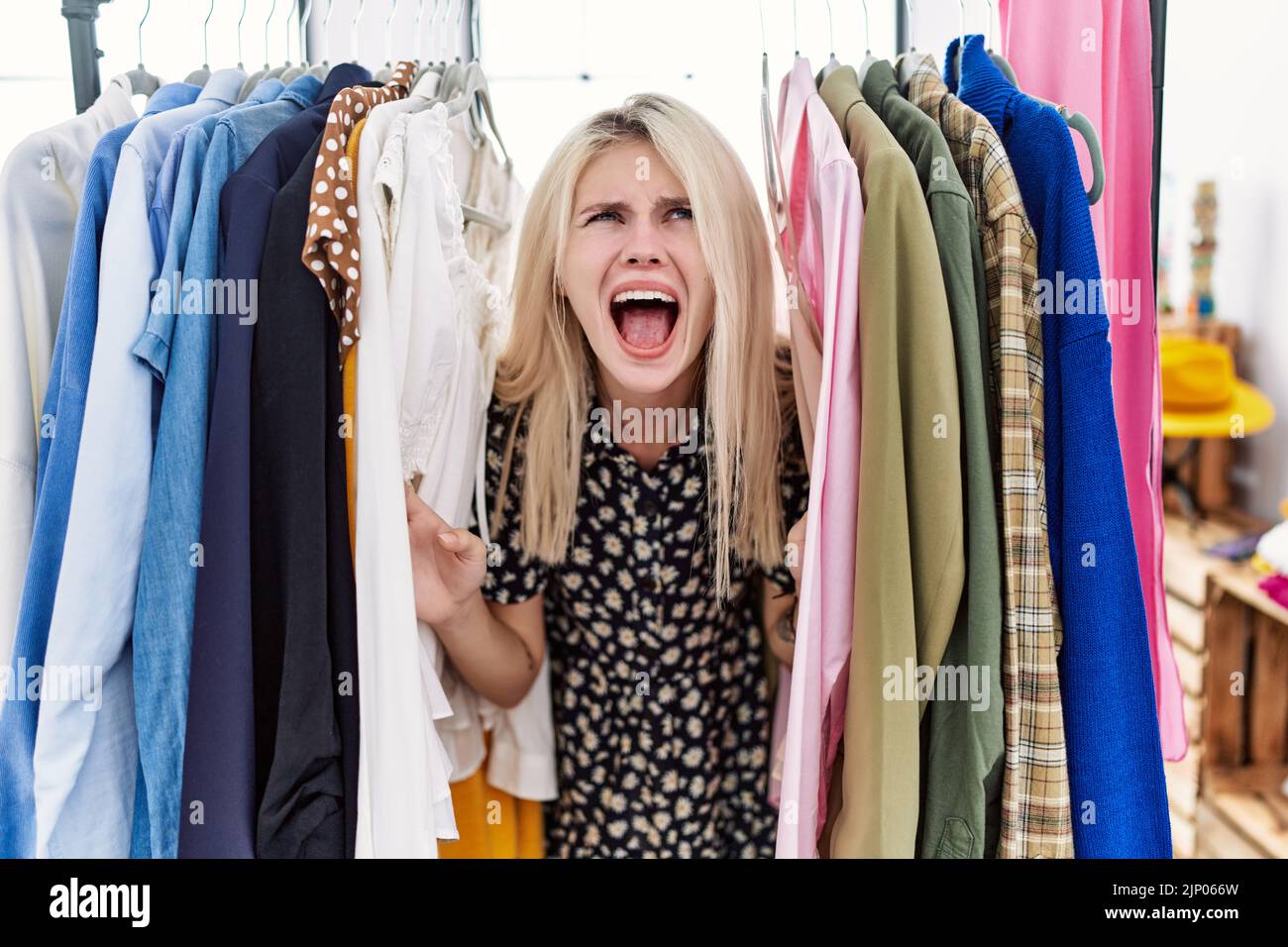 Young blonde woman searching clothes on clothing rack angry and mad ...