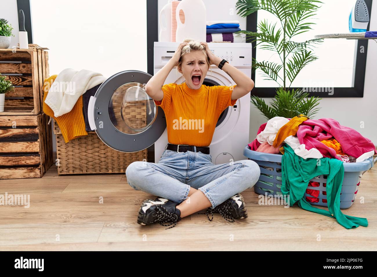 Young blonde woman doing laundry sitting by washing machine crazy and ...