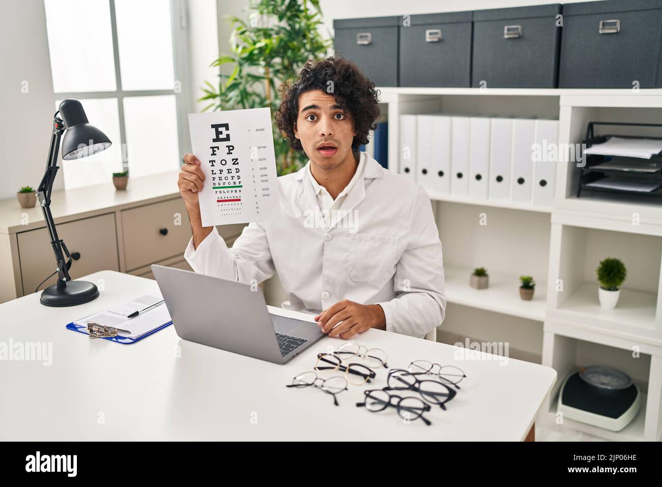 Hispanic man with curly hair holding eyesight medical exam scared and ...
