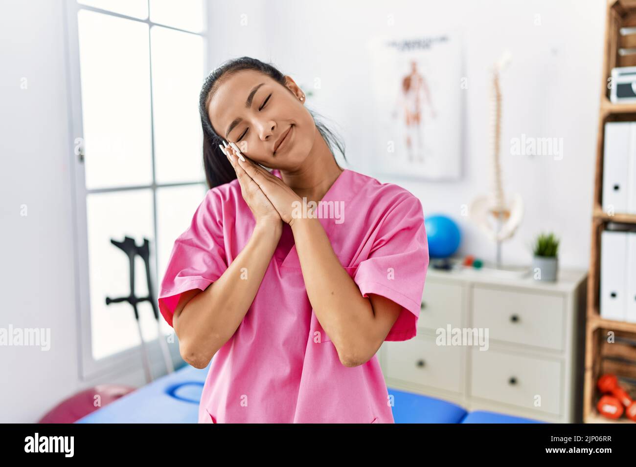 Young hispanic woman working at pain recovery clinic sleeping tired ...
