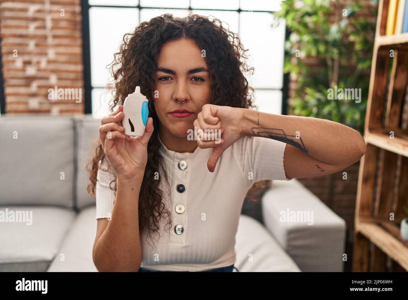 Young hispanic woman using glucose meter with angry face, negative sign ...