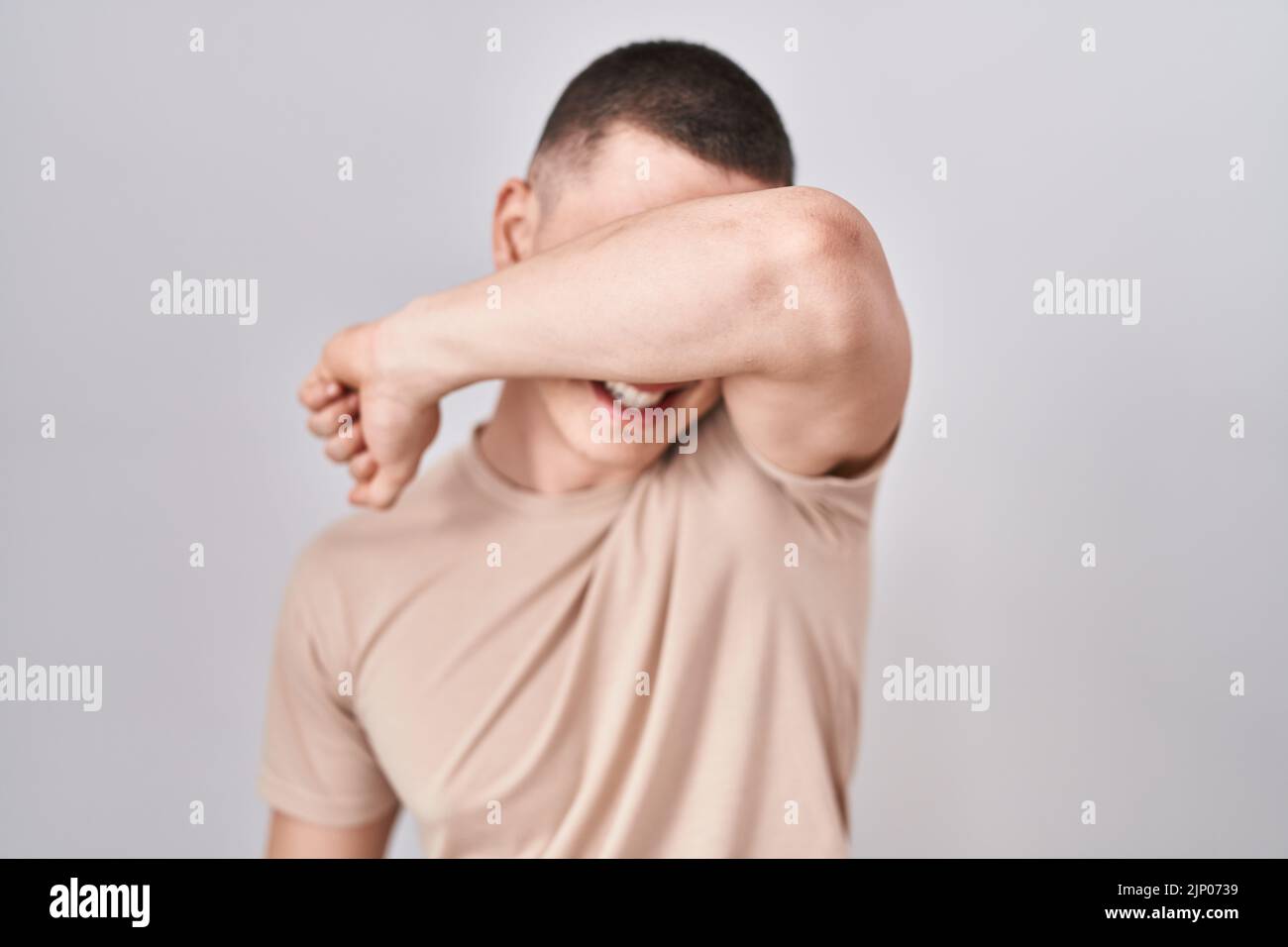 Young man standing over isolated background covering eyes with arm ...