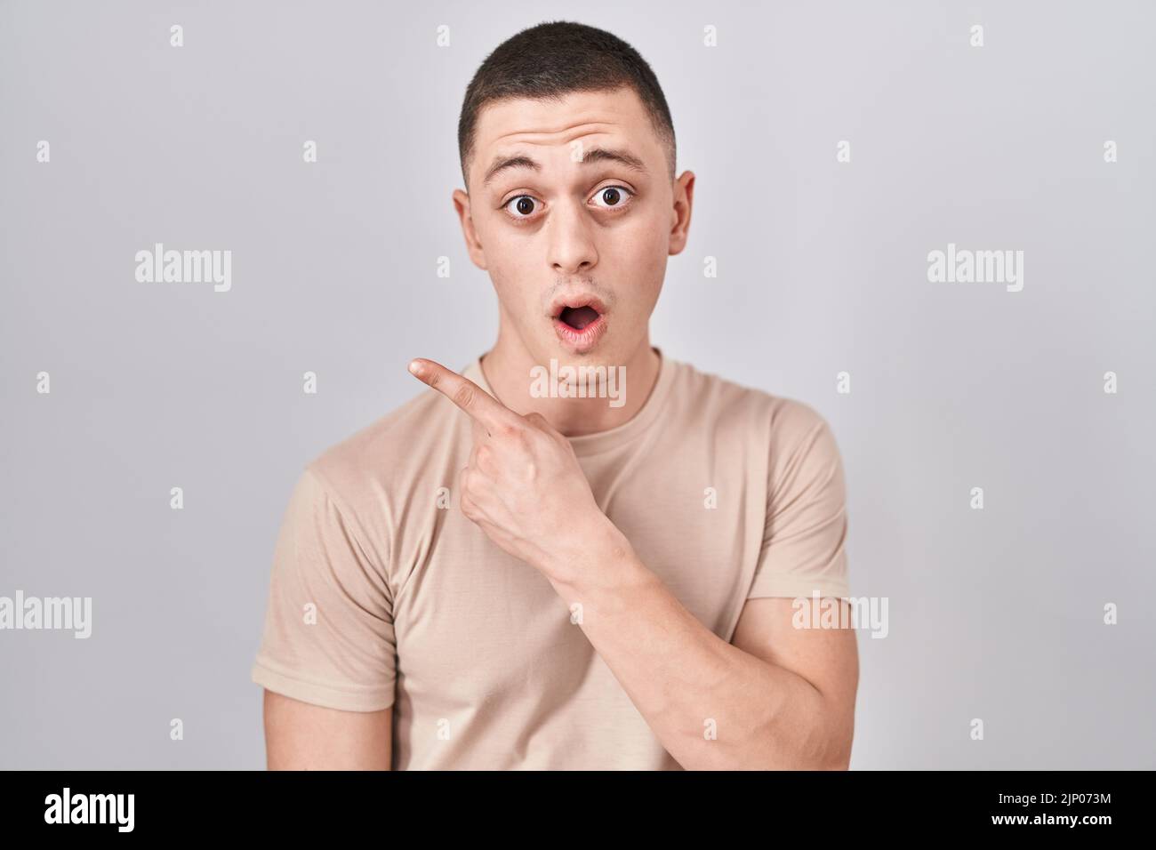 Young man standing over isolated background surprised pointing with ...