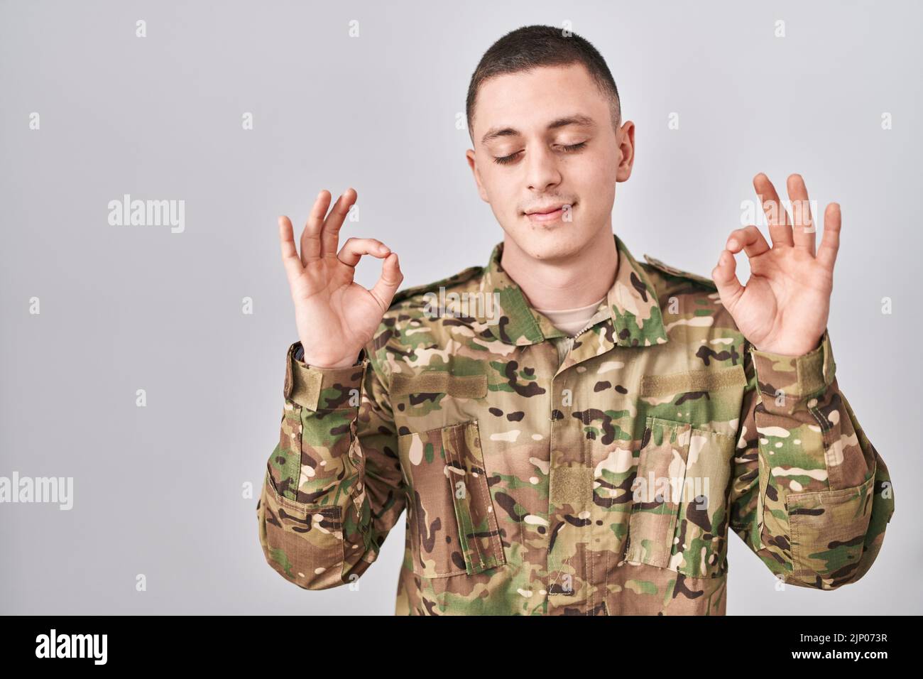 Young man wearing camouflage army uniform relax and smiling with eyes ...