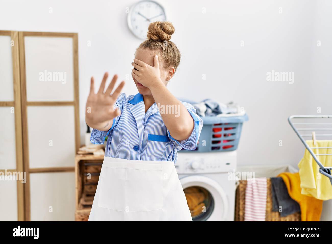 Young caucasian woman wearing cleaner uniform at the laundry room ...