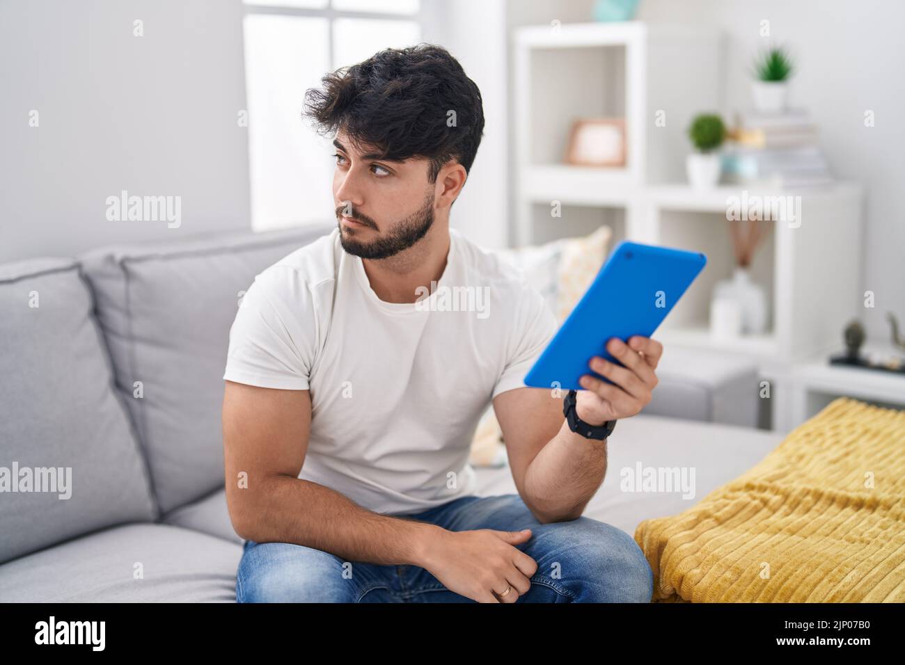 Hispanic man with beard using touchpad sitting on the sofa looking to ...