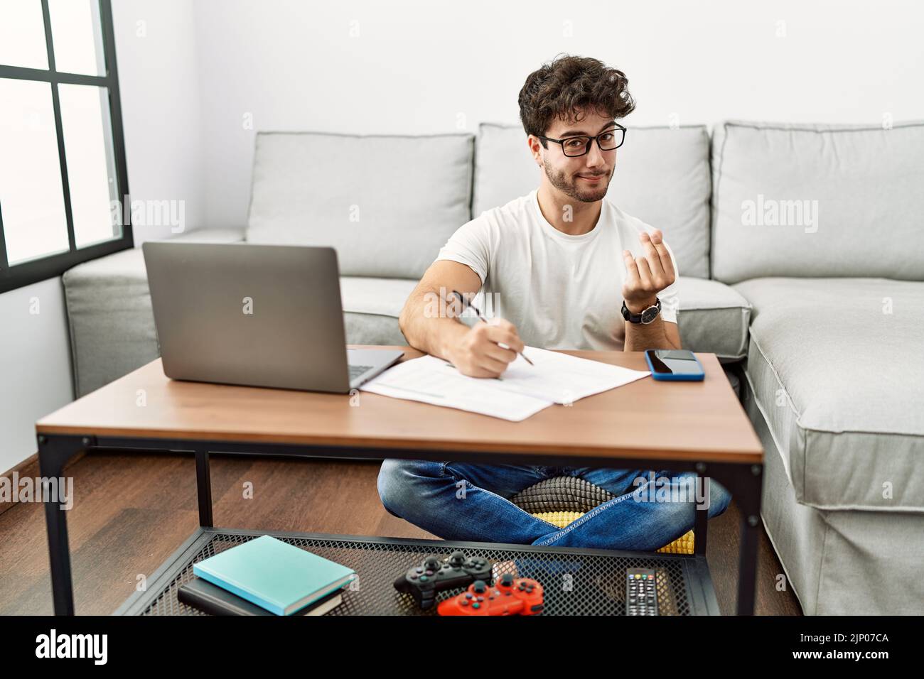Hispanic man doing papers at home doing money gesture with hands ...