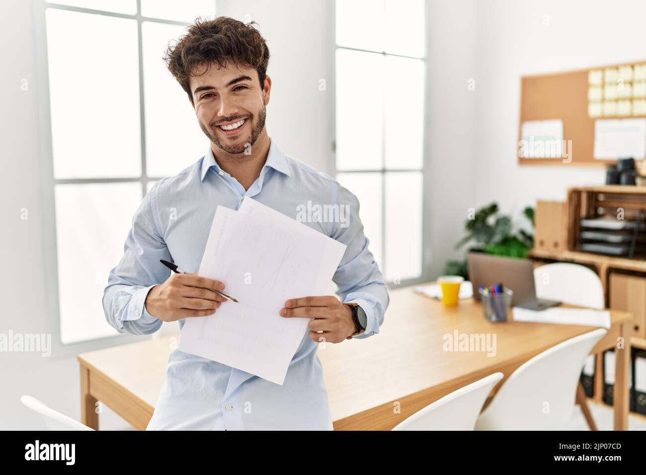 Young hispanic businessman smiling happy holding paperwork standing at ...