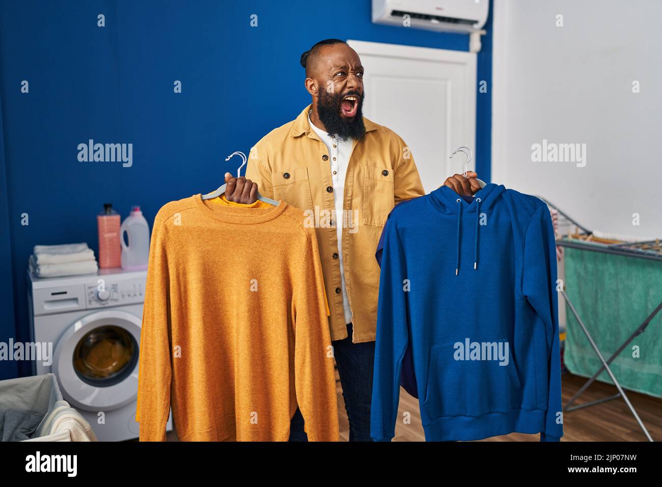 African american man holding clean clothes on hangers at laundry room ...