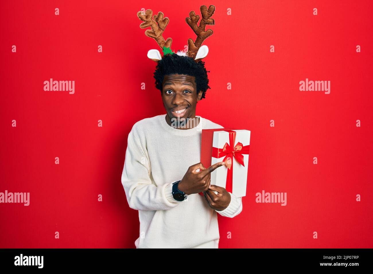 Young african american man wearing deer christmas hat holding gift ...