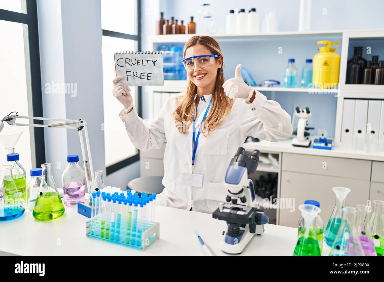 Young blonde scientist woman working on cruelty free laboratory smiling happy and positive ...