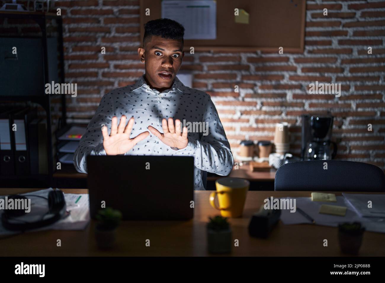 Young hispanic man working at the office at night afraid and terrified ...
