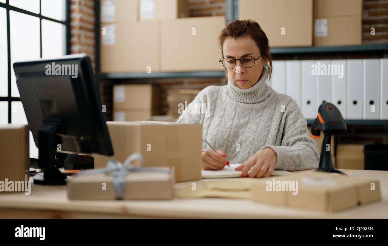Middle age hispanic woman ecommerce business worker writing on book at ...