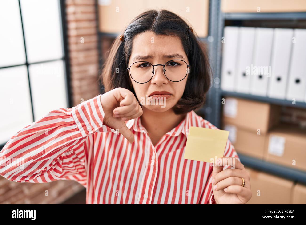 Young hispanic woman holding paper reminder at the office with angry ...