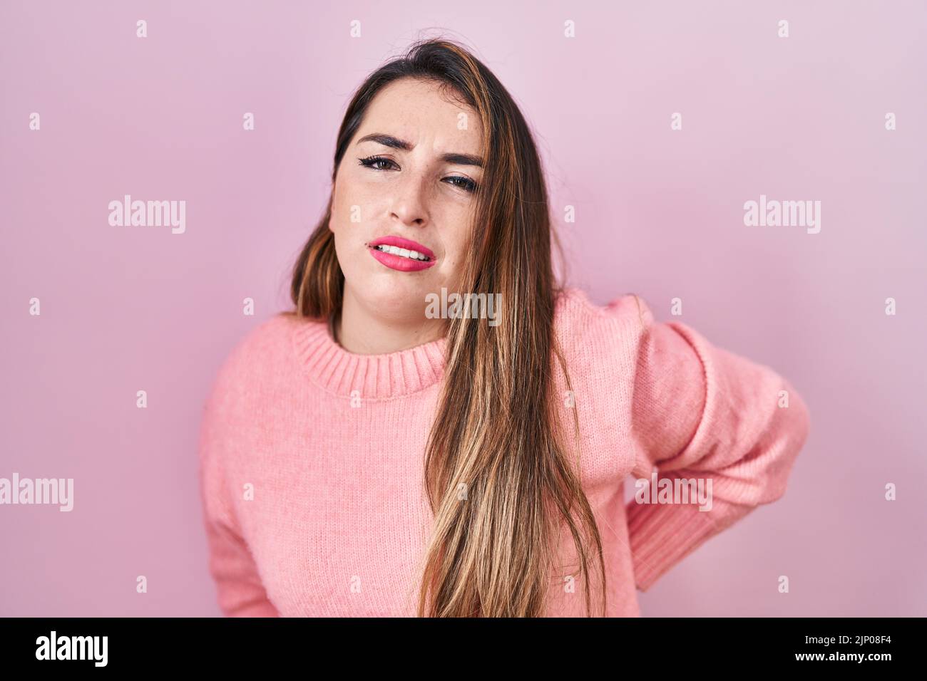 Young hispanic woman standing over pink background suffering of ...