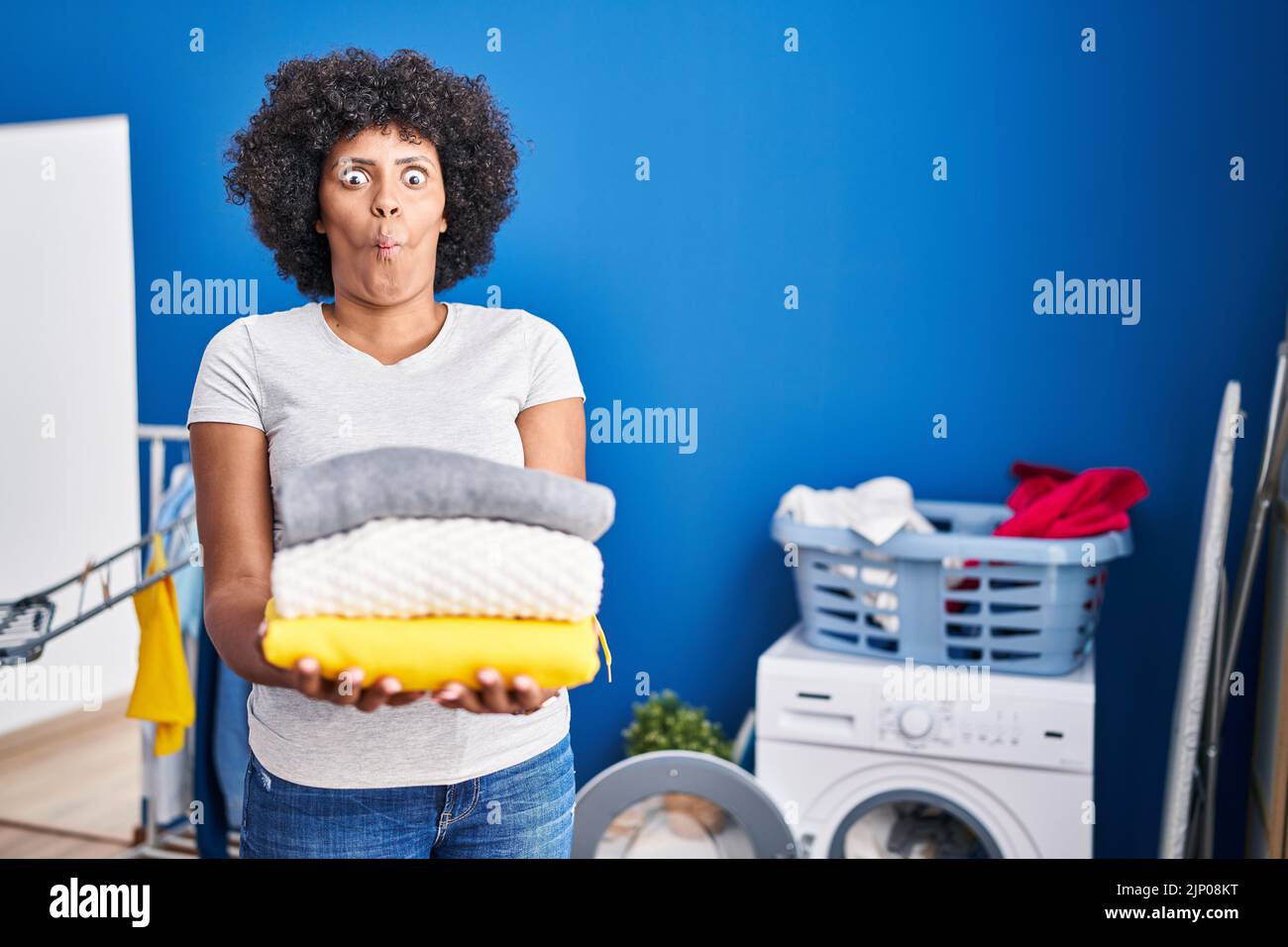 Black woman with curly hair holding clean laundry making fish face with ...