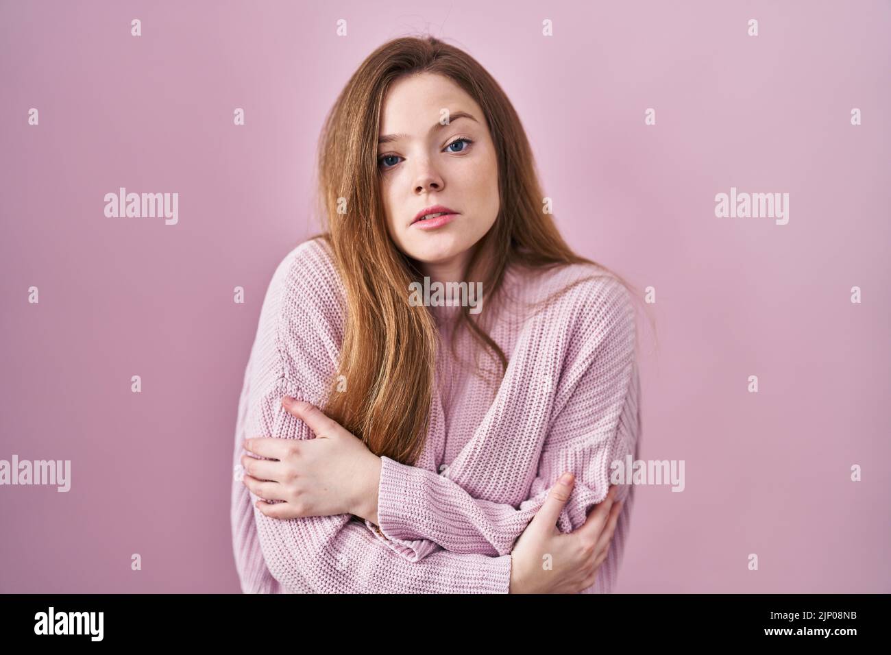 Young caucasian woman standing over pink background shaking and ...