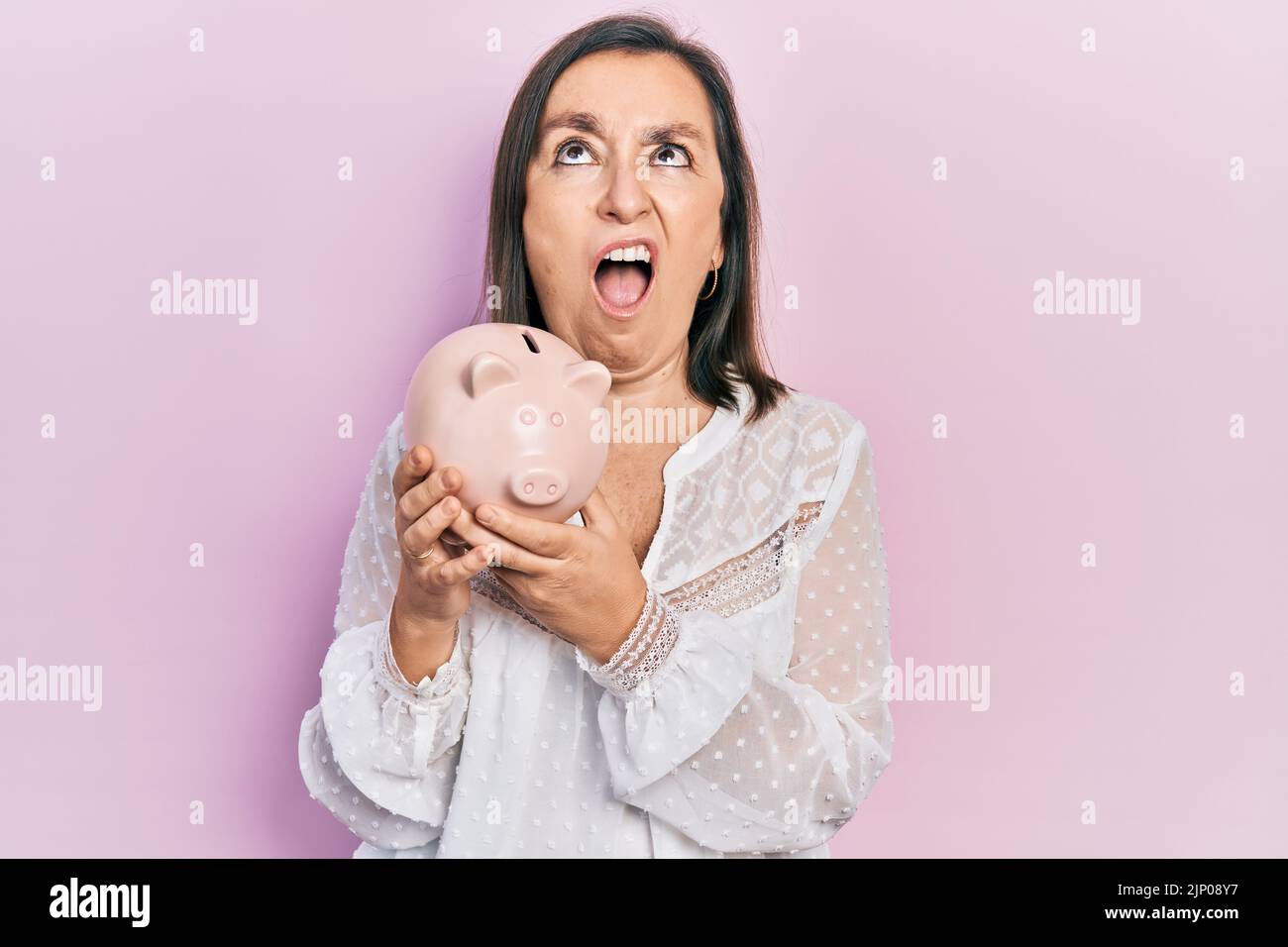 Middle age hispanic woman holding piggy bank angry and mad screaming ...