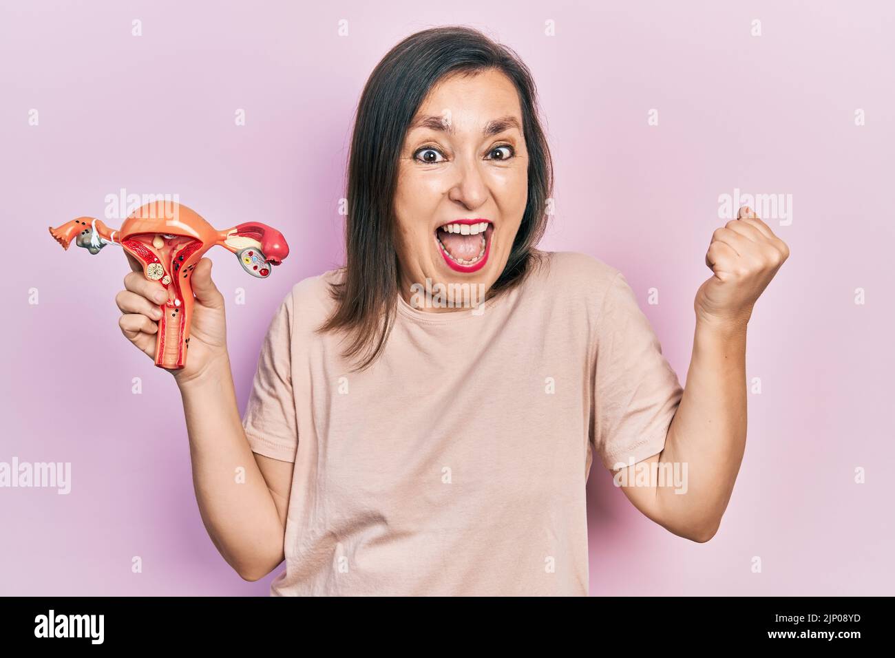 Middle age hispanic woman holding anatomical model of female genital ...