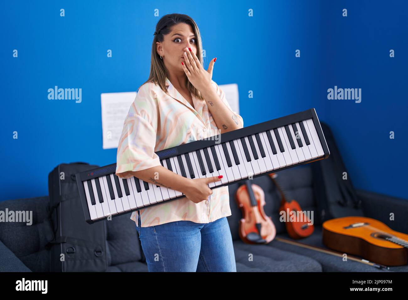 Blonde woman holding piano keyboard covering mouth with hand, shocked ...