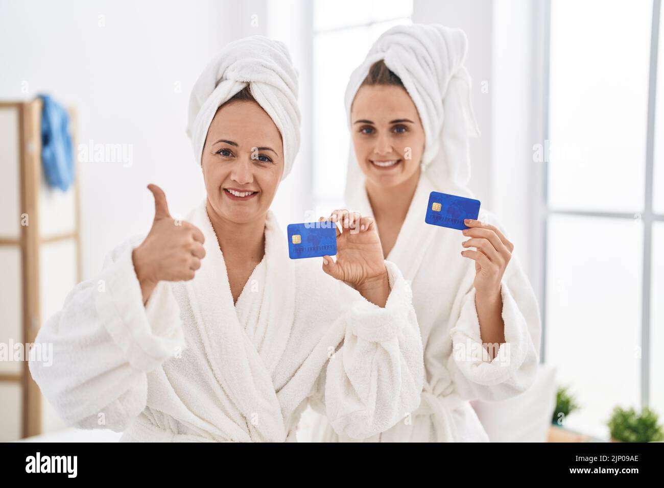 Middle age woman and daughter wearing bathrobe holding credit card ...