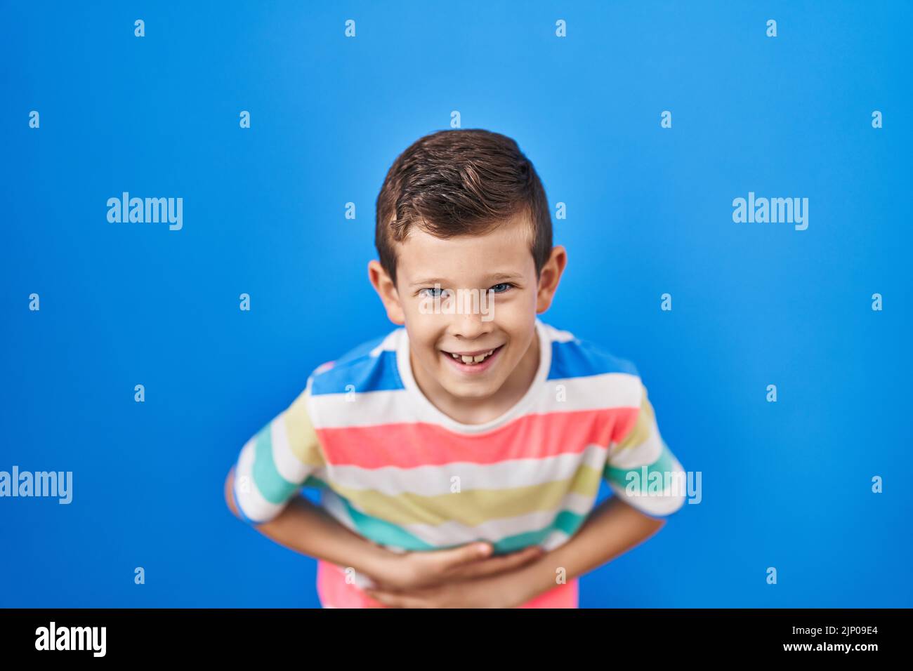 Young caucasian kid standing over blue background smiling and laughing ...