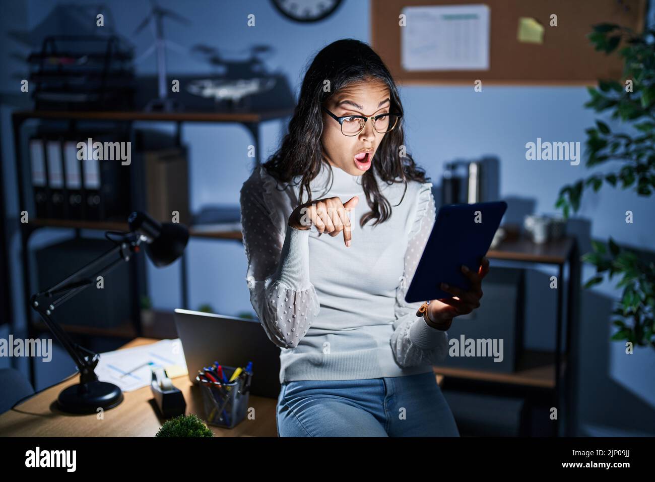 Young brazilian woman using touchpad at night working at the office ...