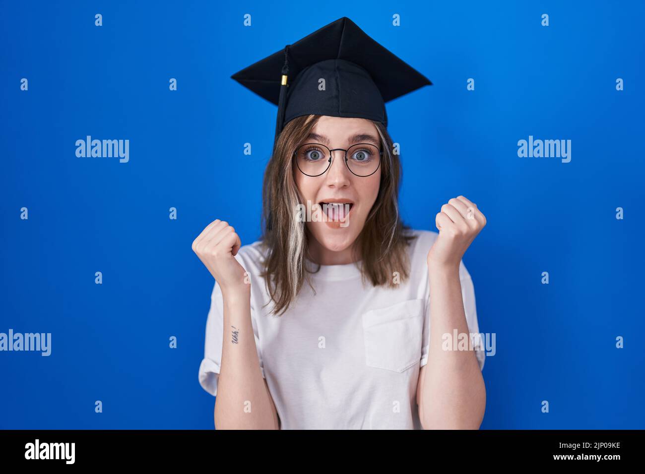 Blonde caucasian woman wearing graduation cap celebrating surprised and ...