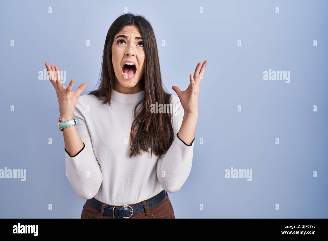 Young brunette woman standing over blue background crazy and mad ...