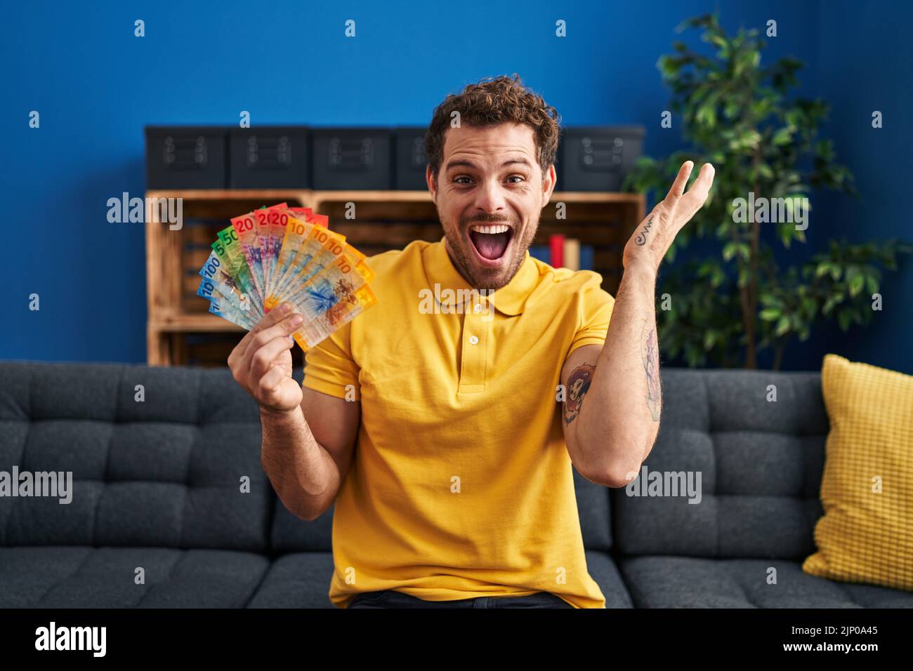 Young hispanic man holding swiss franc banknotes celebrating victory ...
