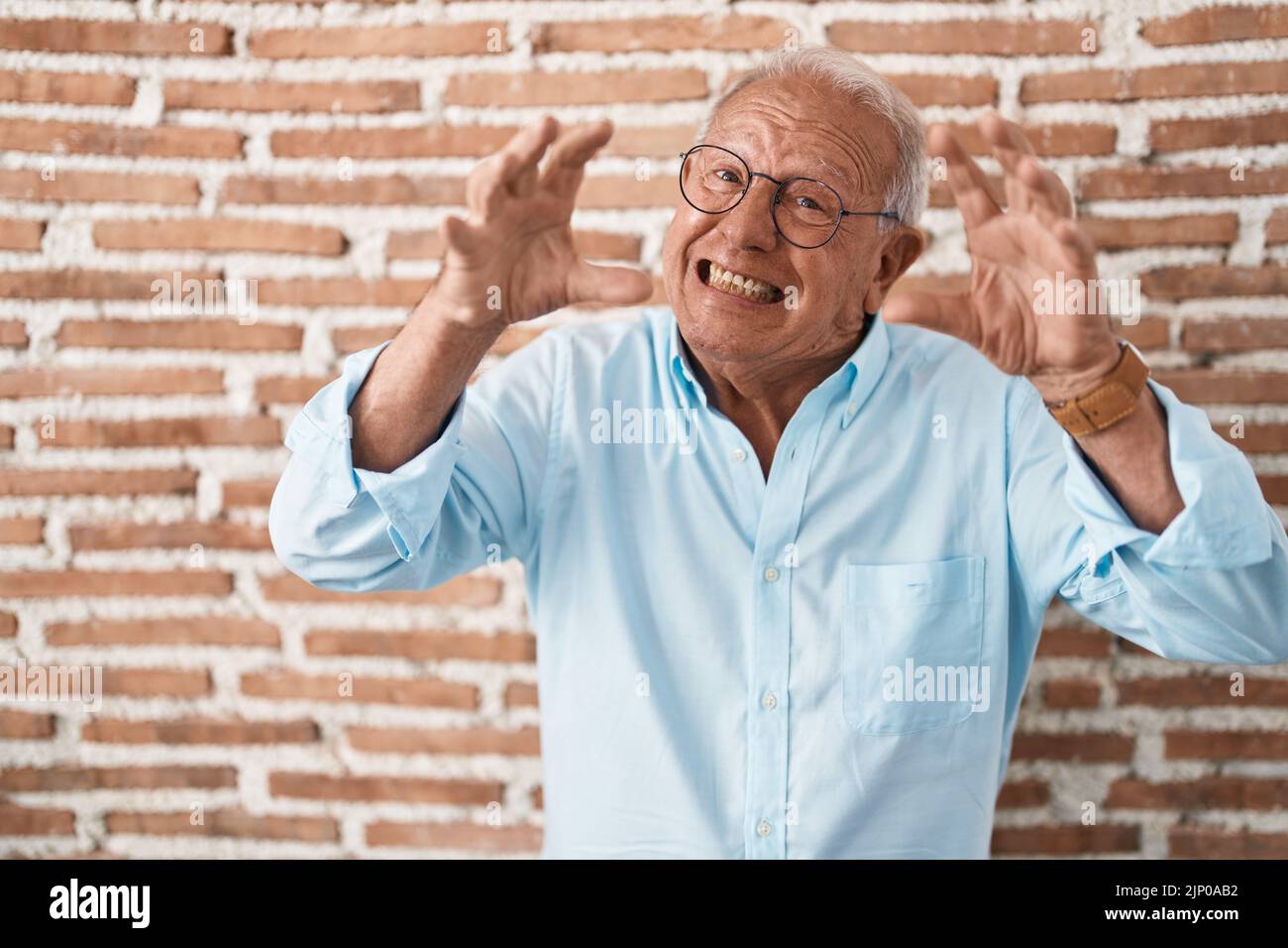 Senior man with grey hair standing over bricks wall shouting frustrated ...