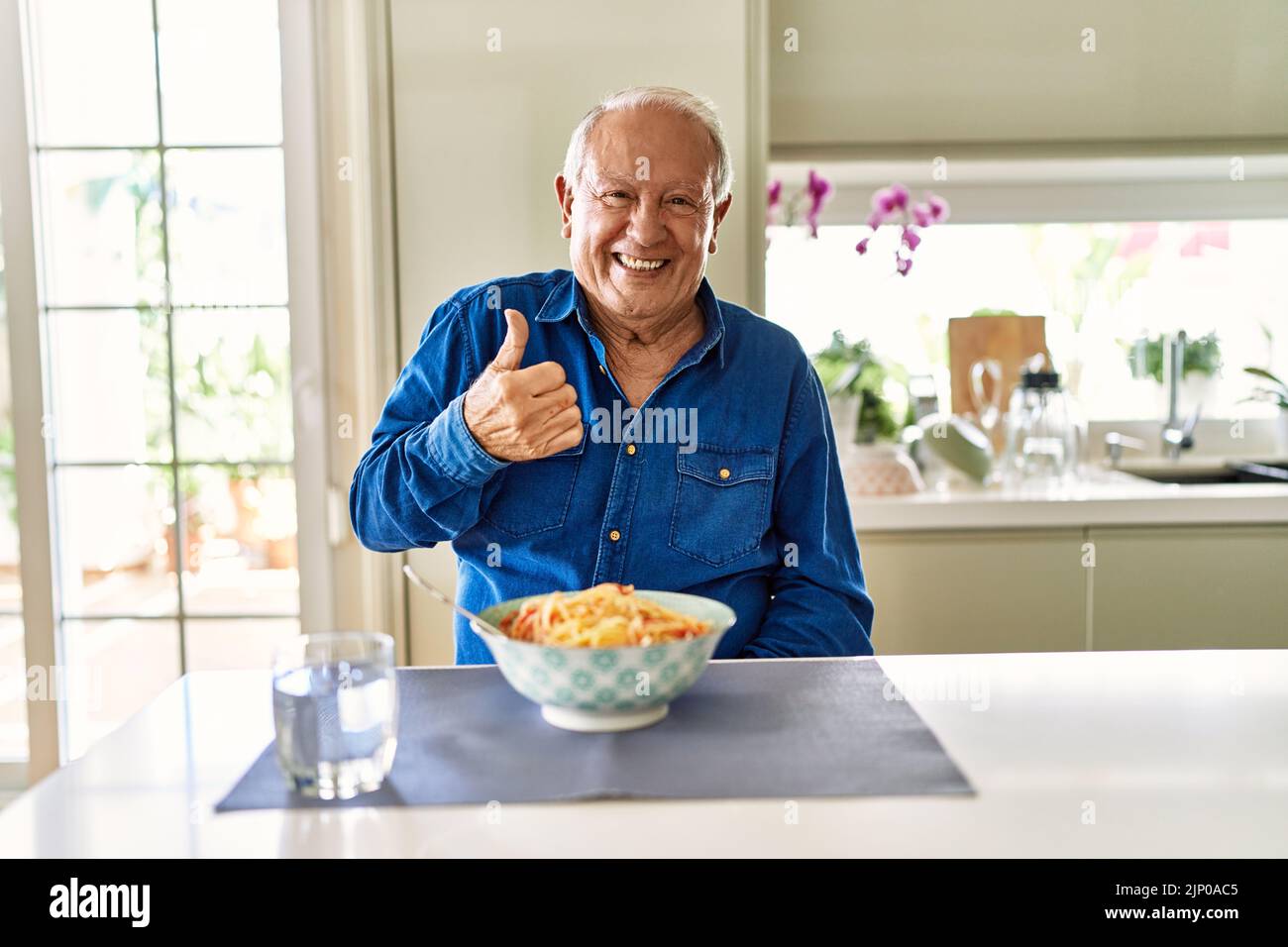 Senior man with grey hair eating pasta spaghetti at home doing happy ...