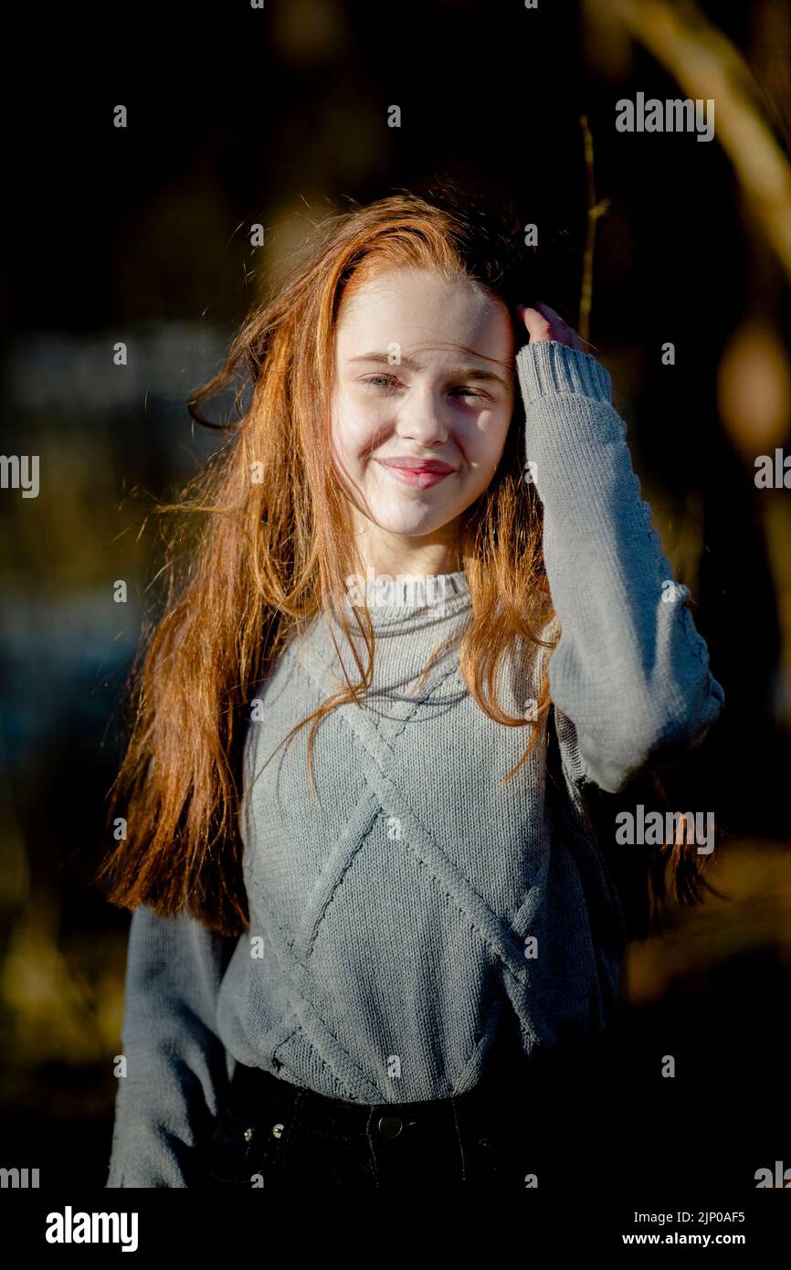 A teenage girl with fiery red long hair poses in the park for a ...