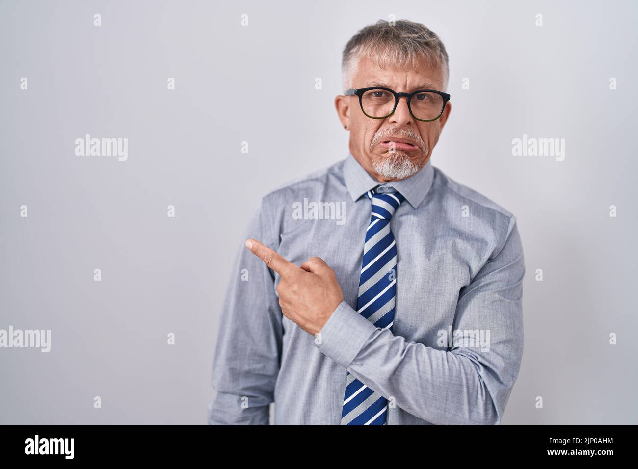 Hispanic business man with grey hair wearing glasses pointing aside ...