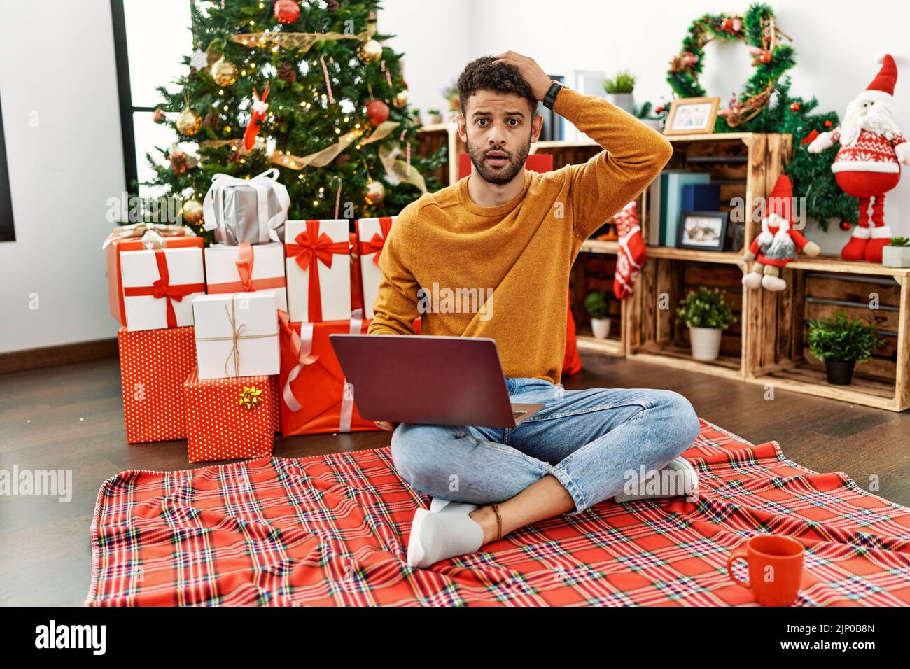 Arab young man using laptop sitting by christmas tree crazy and scared ...